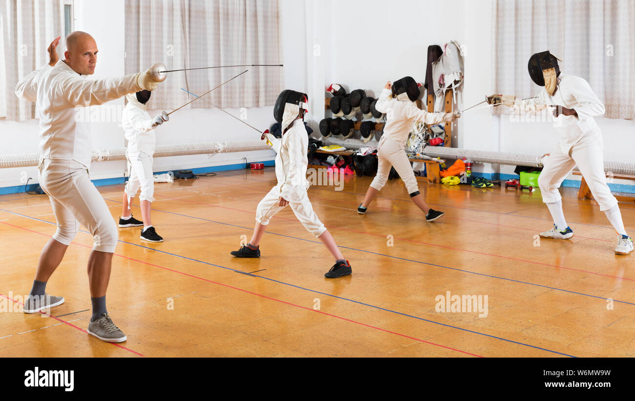 Coach demonstrating to young athletes stances and movements with rapier ...