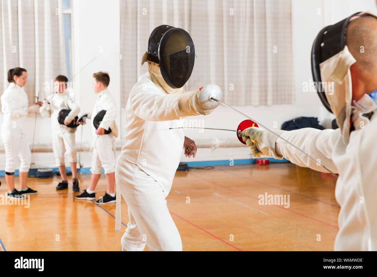 Adults and teens wearing a fencing uniform practicing with foil at a ...