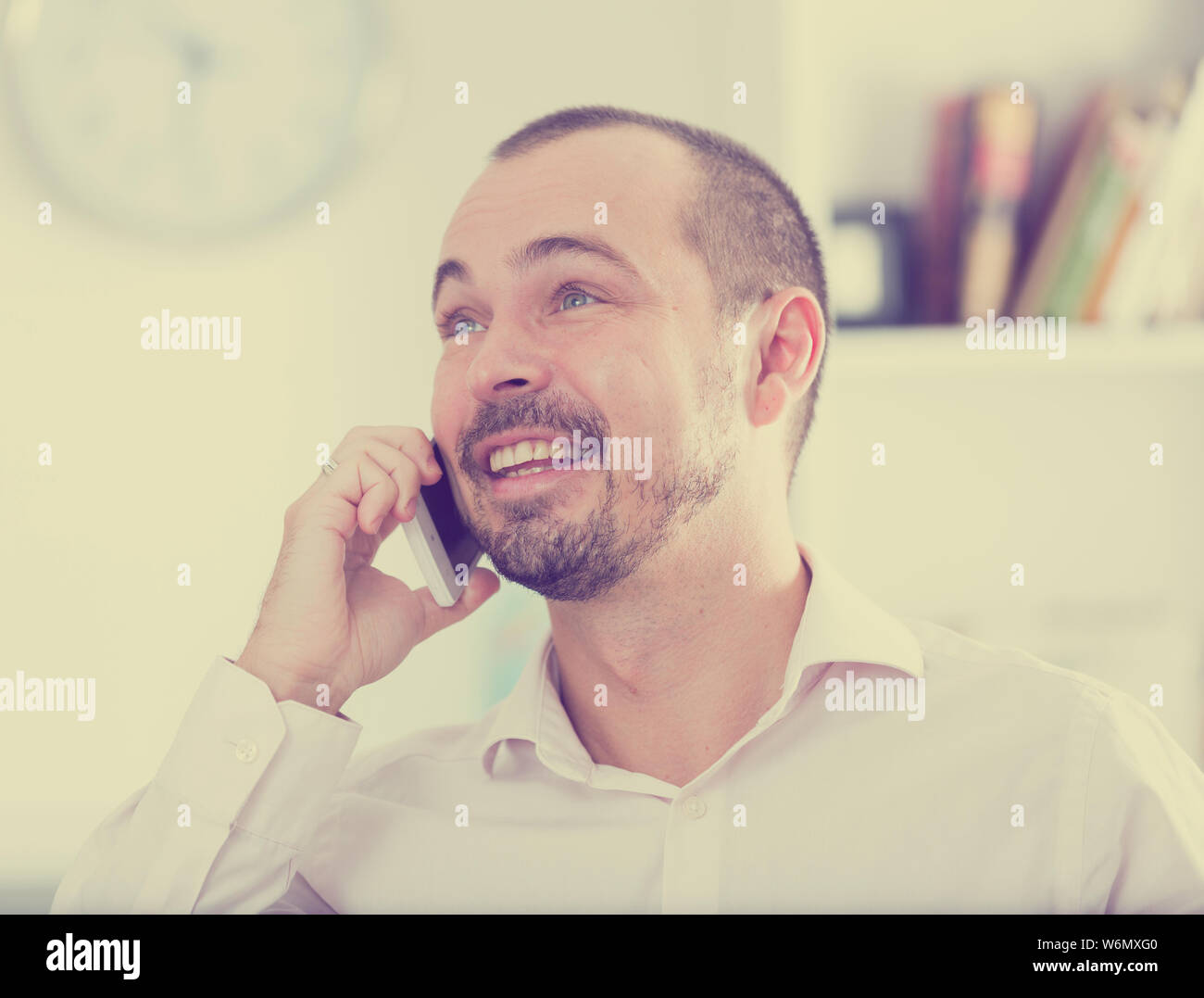 Positive young man texting and calling by smartphone at his workplace ...