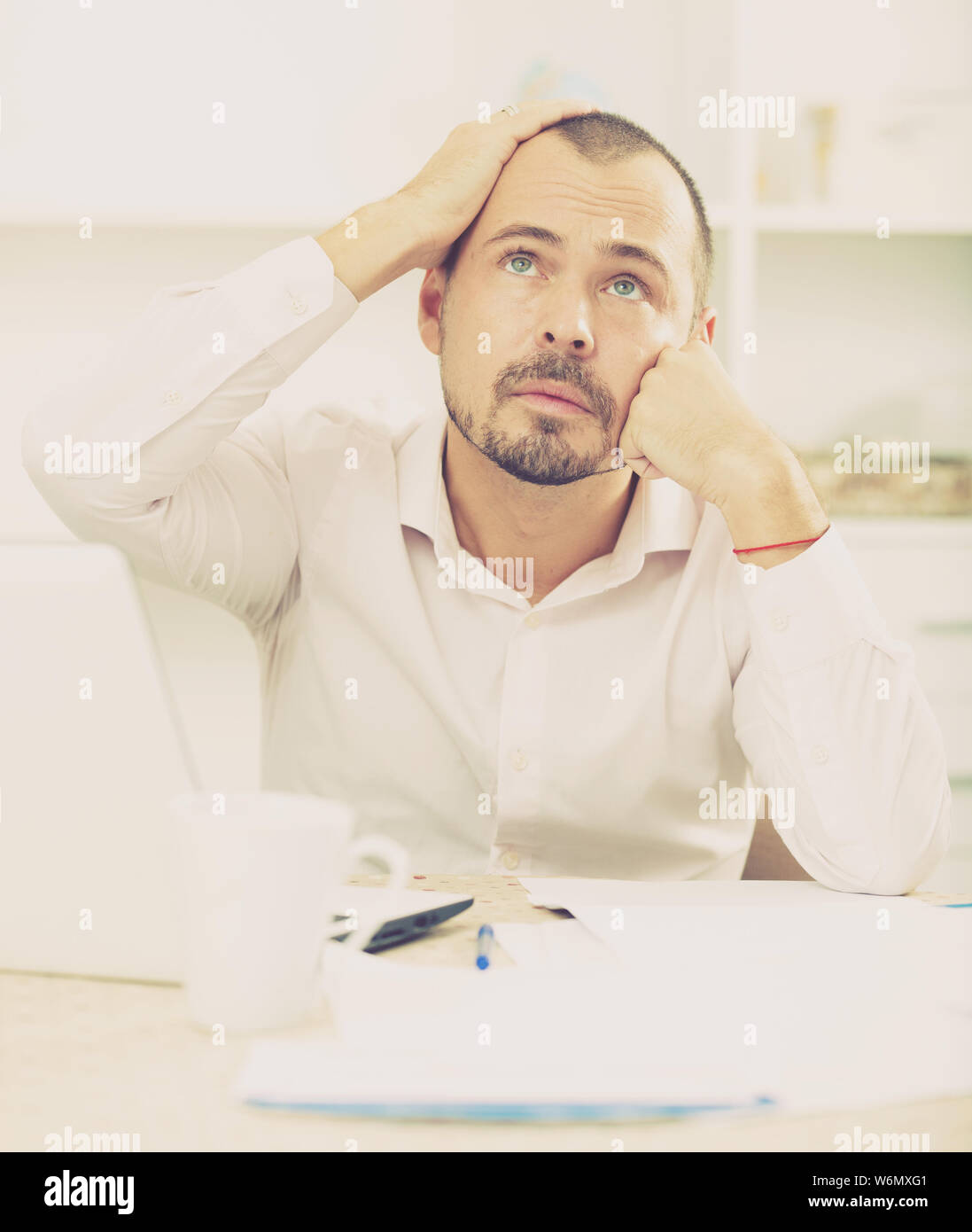 Disappointed worker at his office table feeling stressed, thinking and ...