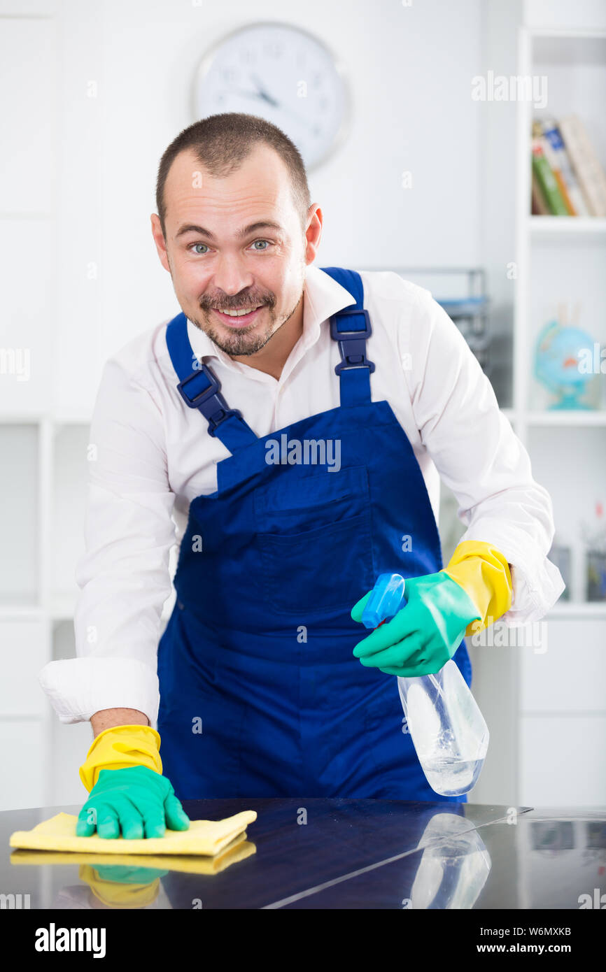 Positive young man in apron cleaning his office desk by cleanser Stock ...