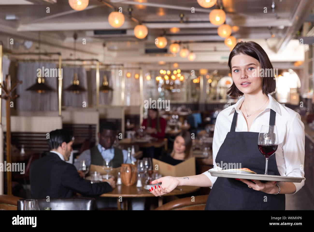Portrait of smiling waitress with serving tray meeting restaurant ...