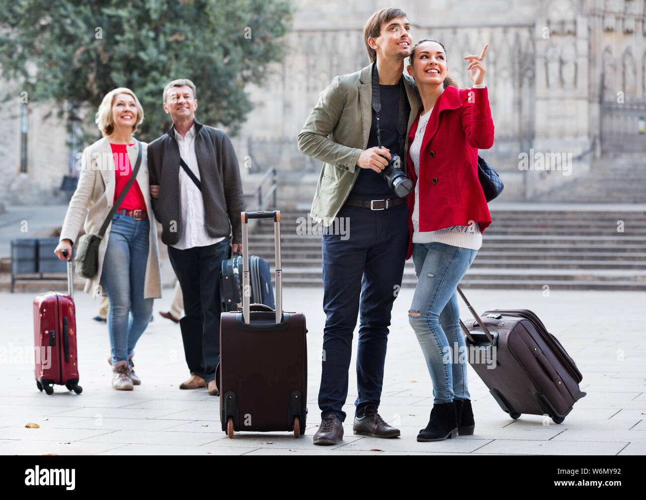 Two positive couples with baggage sightseeing and smiling in spring ...