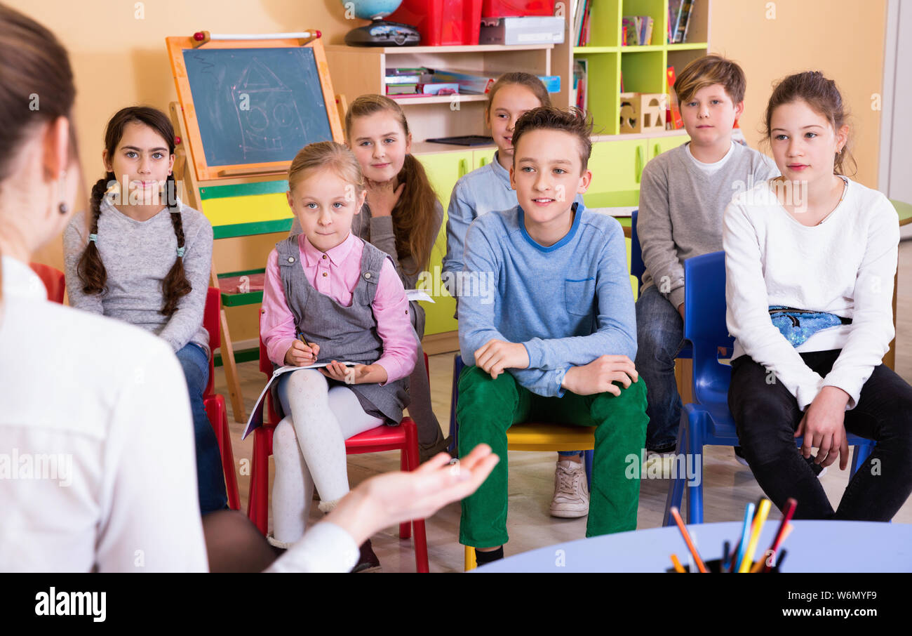 Portrait of diligent smiling positive pupils listening teacher at ...