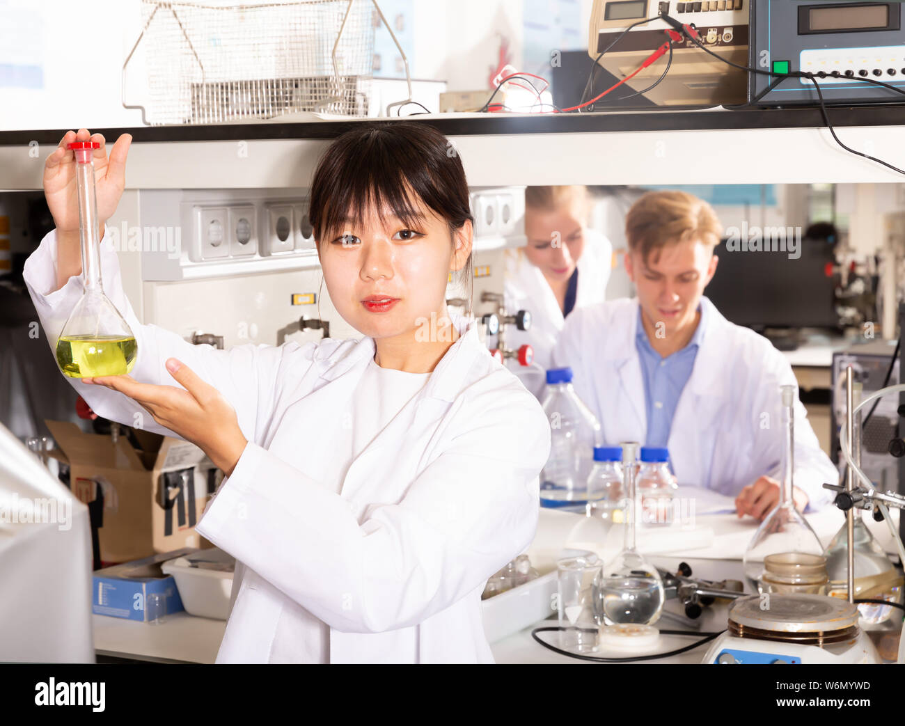 Young Chinese female scientist holding flask of reagent at biochemical ...