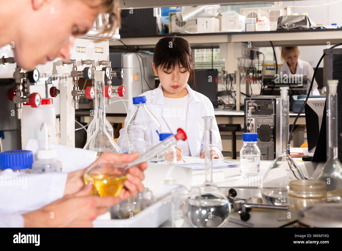 Adult Chinese female student noting results of research at chemical lab ...