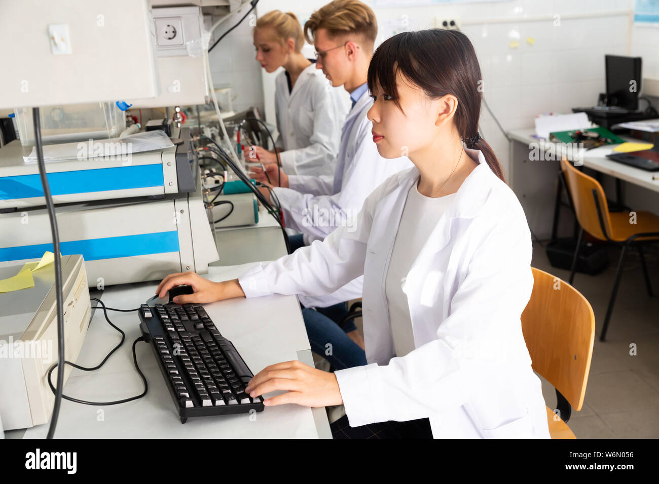Multiracial team of chemists performing experiments on lab equipment in ...