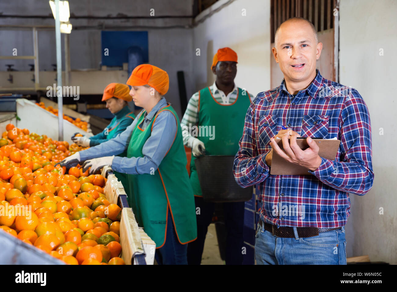 Satisfied diligent cheerful smiling owner of fruit warehouse standing ...