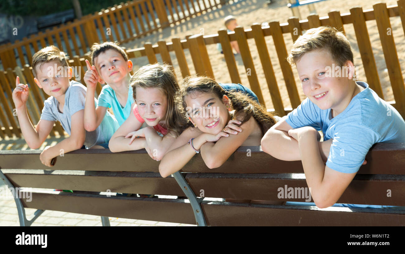 Five glad children sitting on a bench at the playground and point to ...
