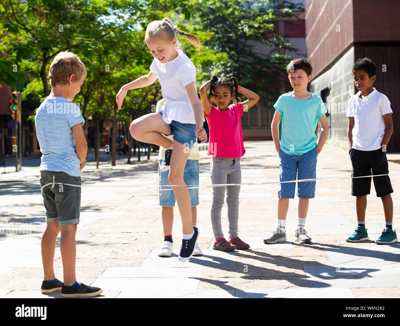 Energetic kids playing and skipping on elastic jumping rope in european ...