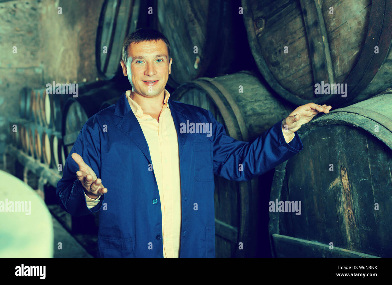 Happy worker of winery posing with wine barrels in cellar Stock Photo ...