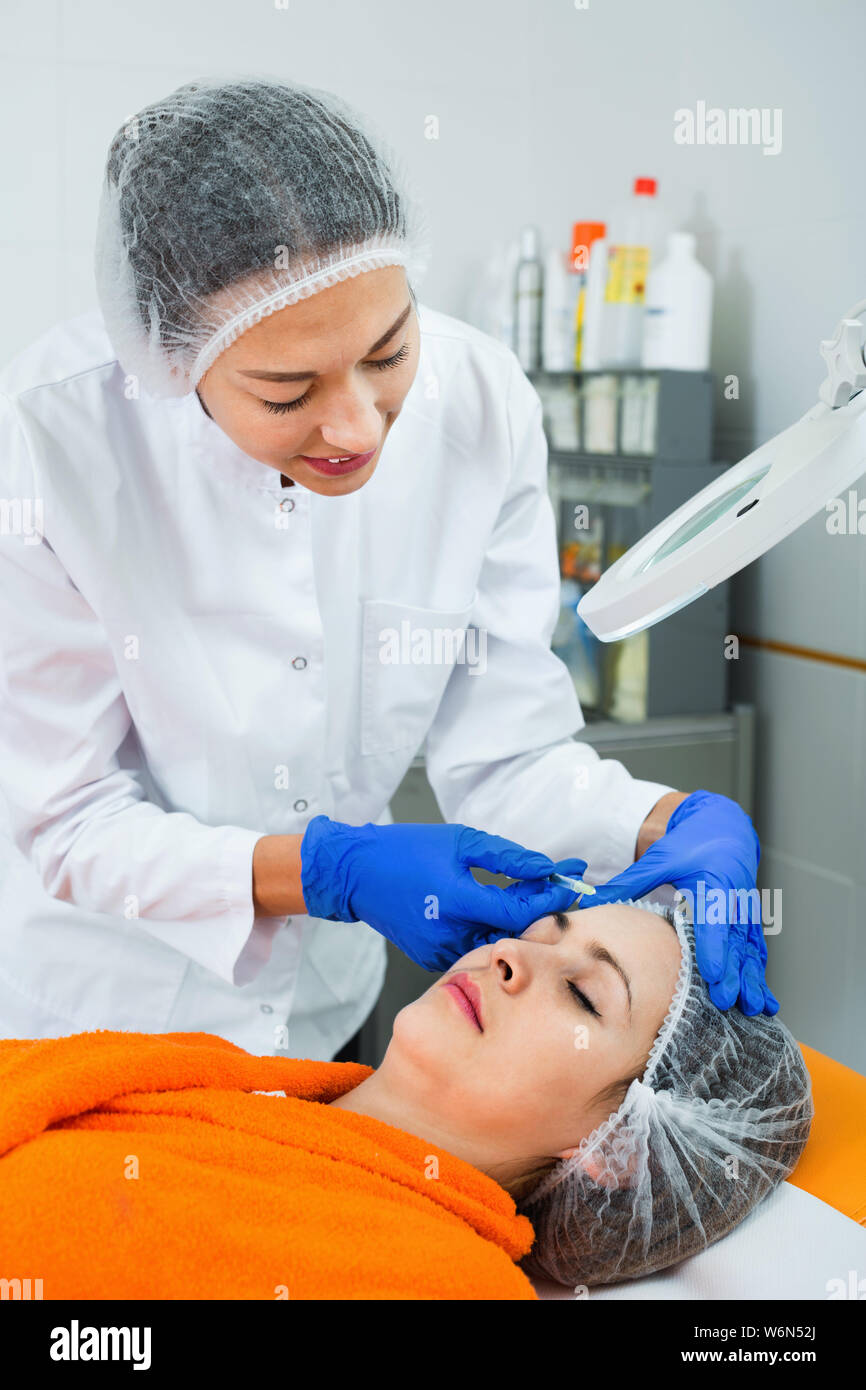 Smiling efficient female doctor doing beauty injection to young woman ...