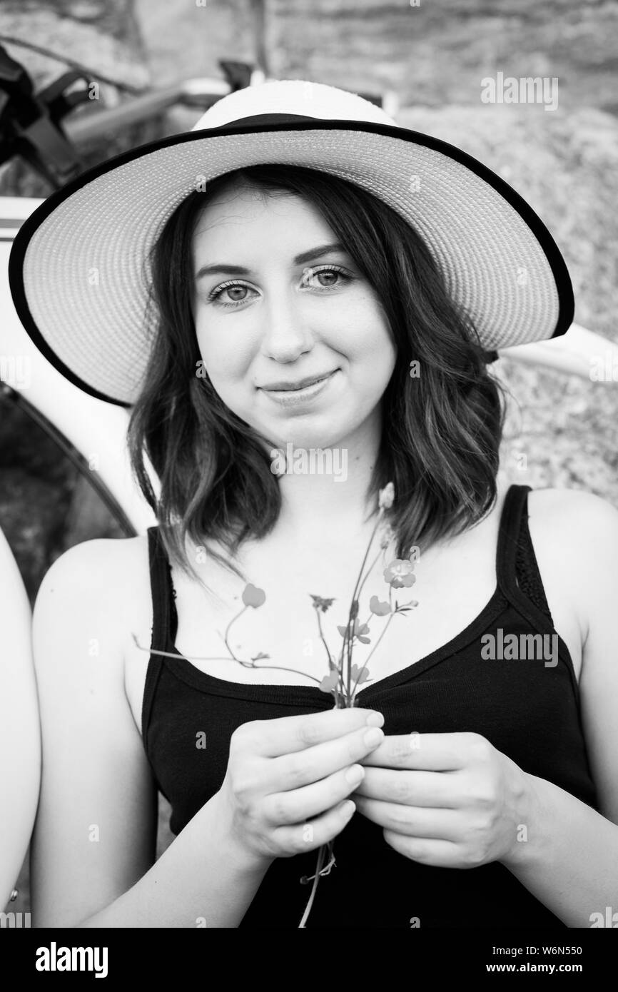 pretty girl in sun hat looking at camera, smiling, flowers in hands ...