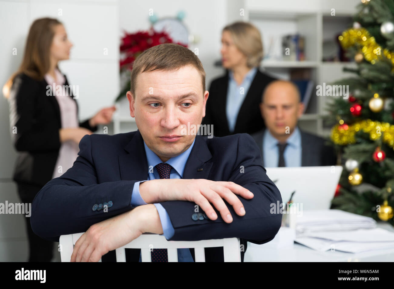 Upset businessman sitting in office with working colleagues behind ...