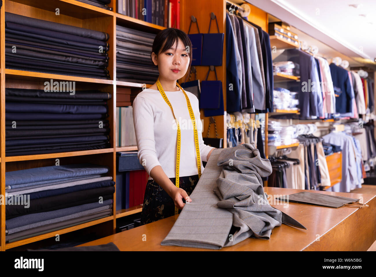 Glad Chinese salesgirl working in fabric store, demonstrating wide ...