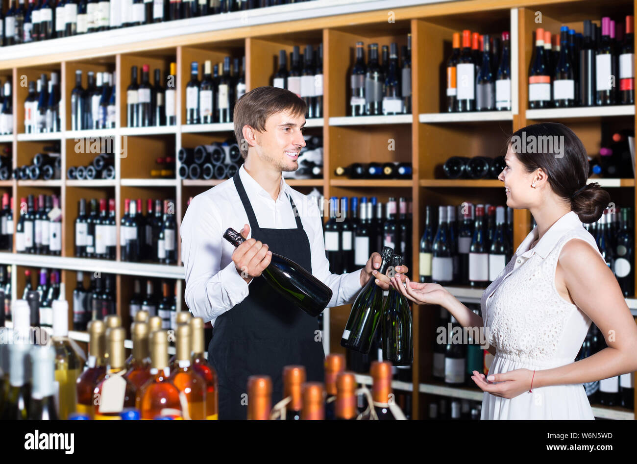 portrait of happy spanish male seller in uniform showing bottle of wine ...
