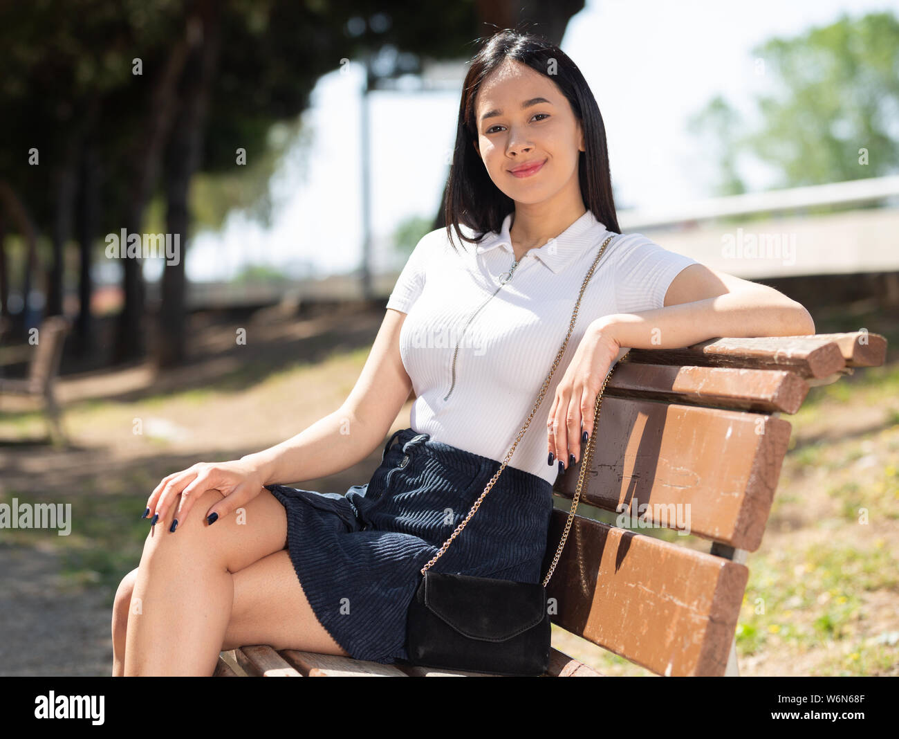 Smiling teenager girl sitting on a bench in city park Stock Photo - Alamy