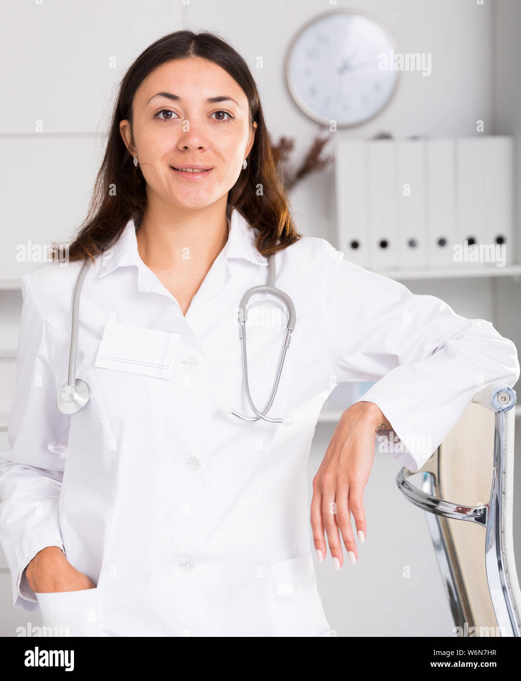 Portrait of young female practitioner in white uniform standing in ...