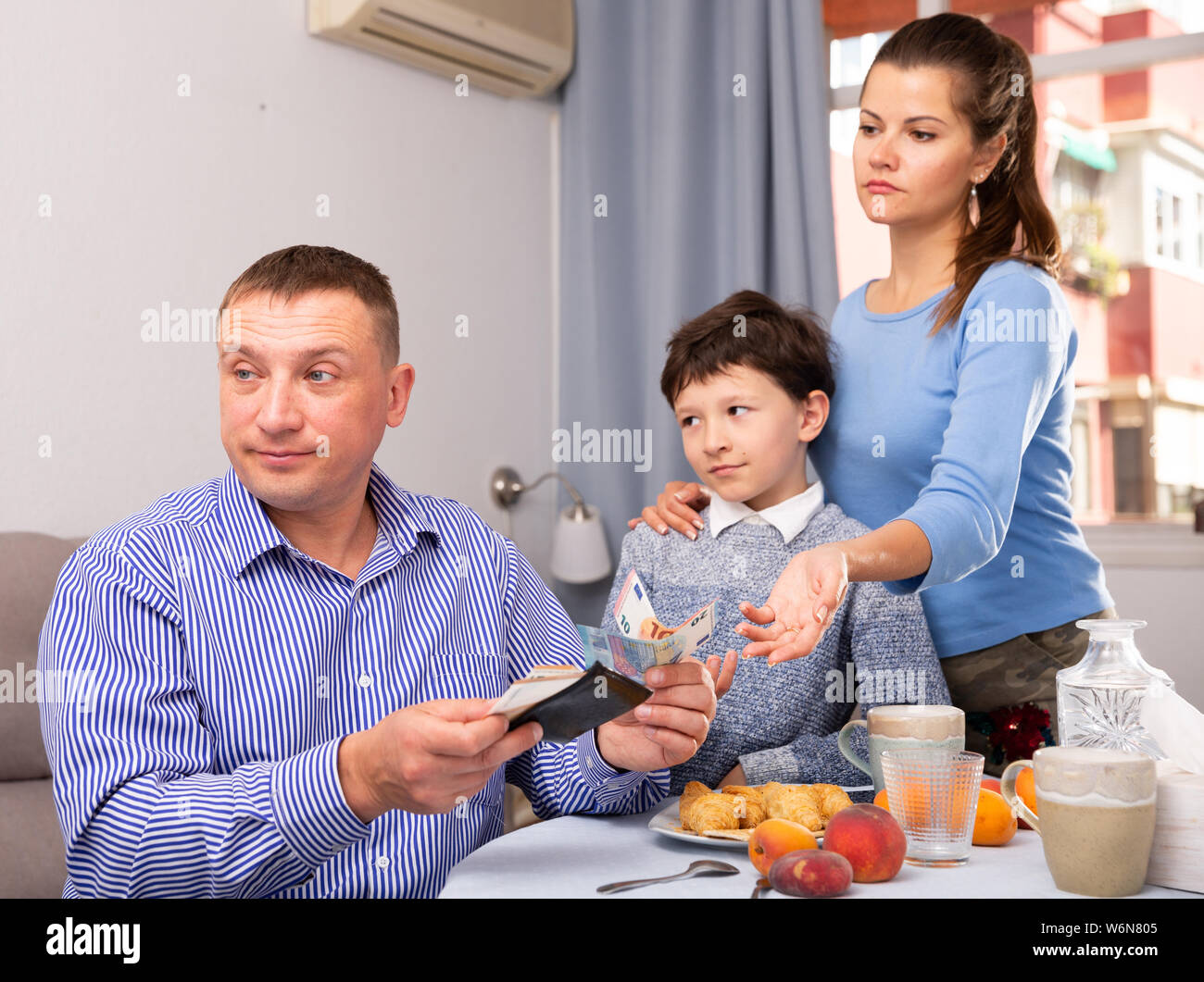 Upset father giving pocket money to his wife and preteen son at home ...