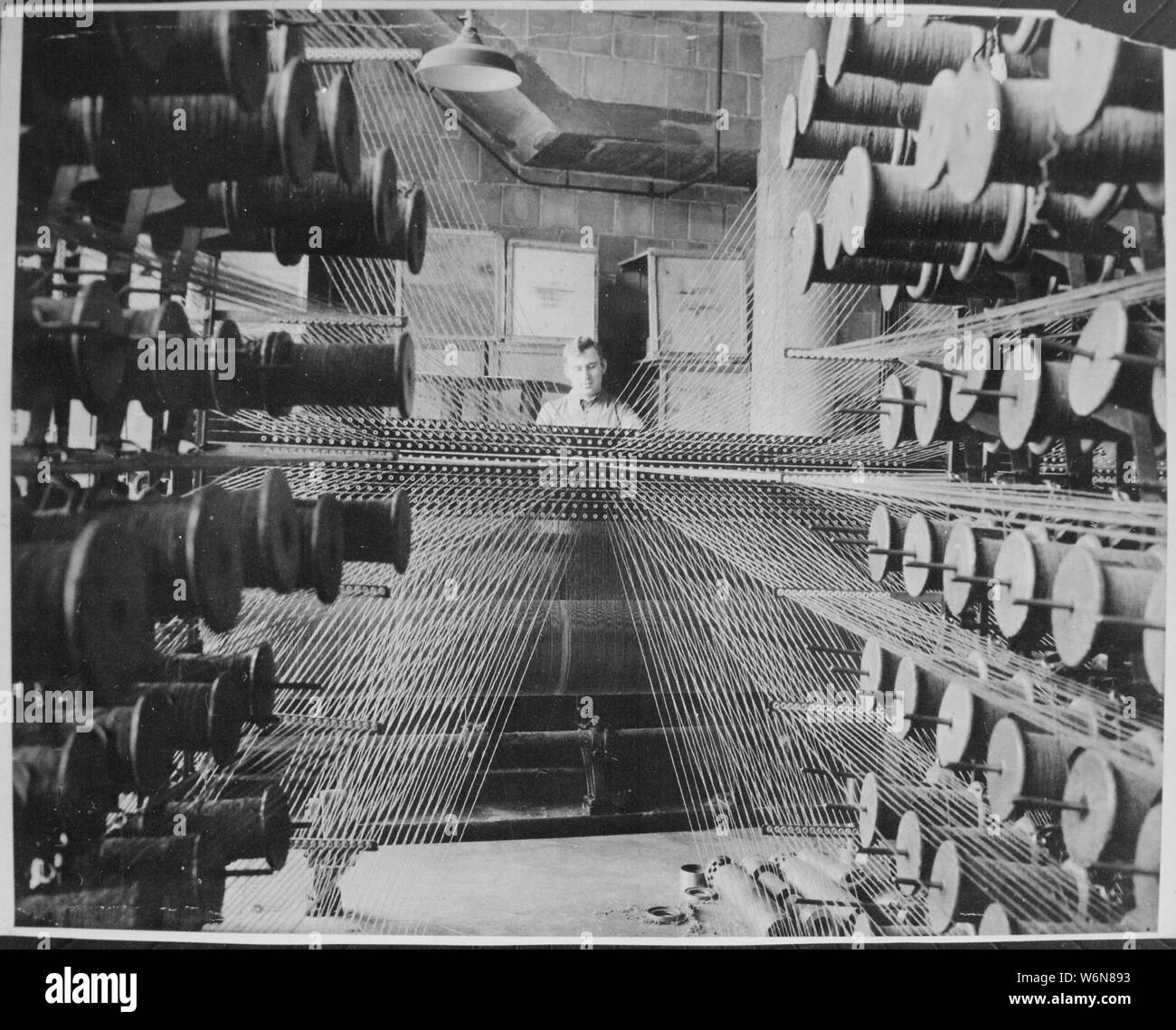 Workman operating an industrial loom strung with hundreds of wool ...