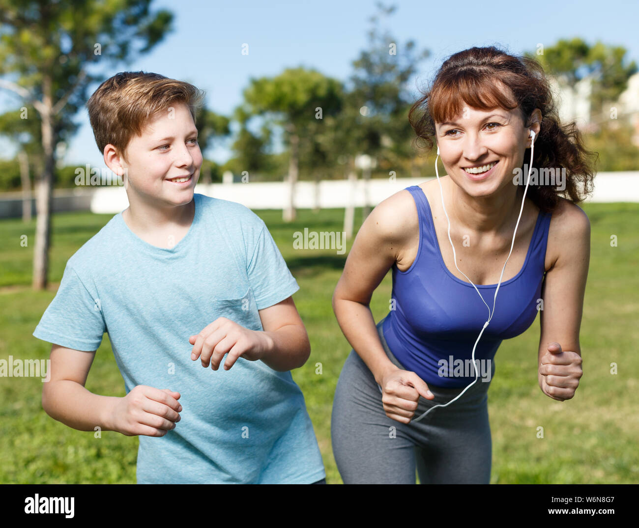 Portrait of young athletic woman with earphones and tween boy running ...