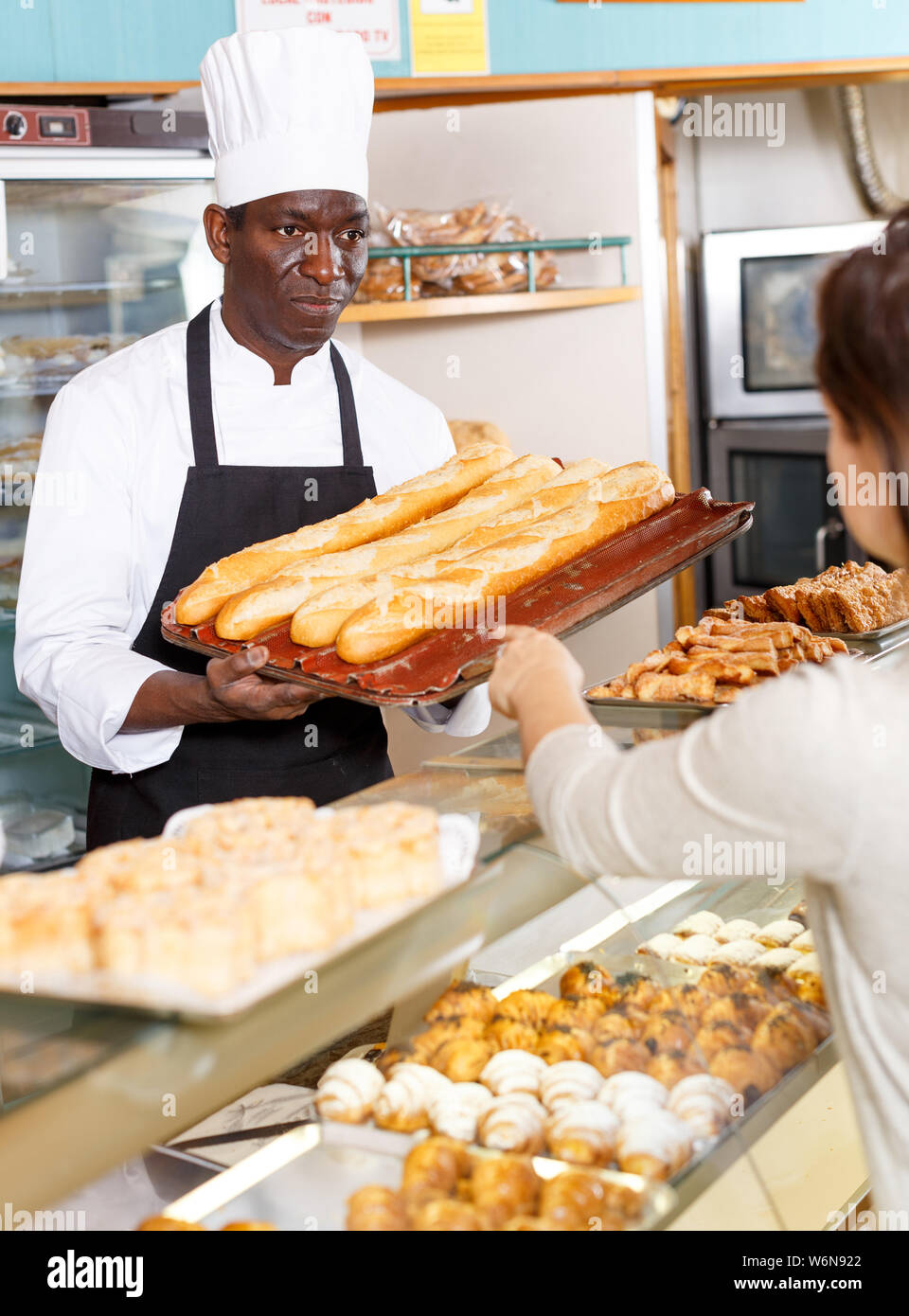 Professional baker standing at counter in bakehouse, selling baked ...