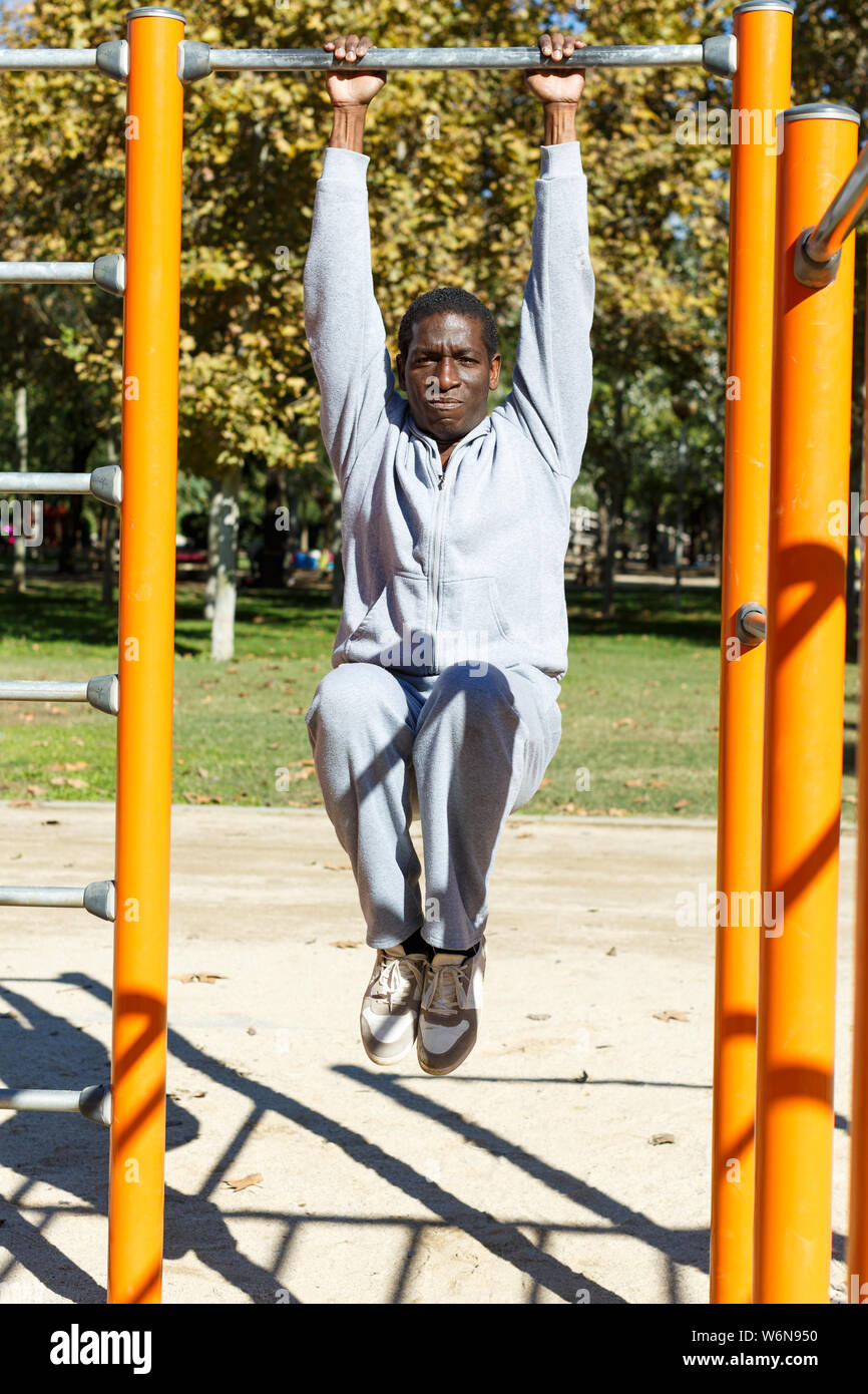 Athletic young male training different exercises at chin-up bar in park ...