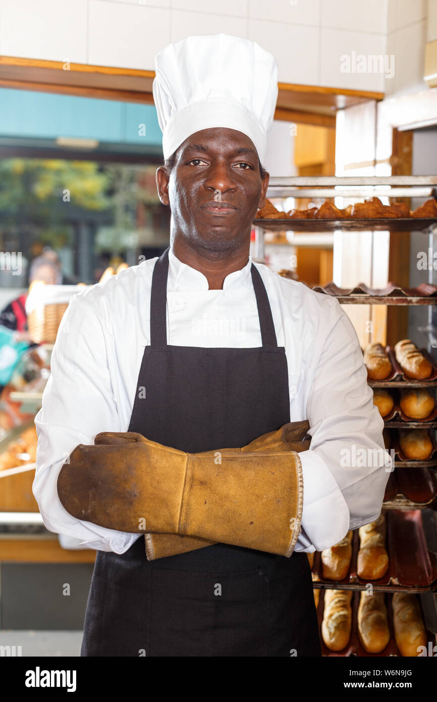 Confident worker of bakery wearing uniform and heat resistant gloves ...