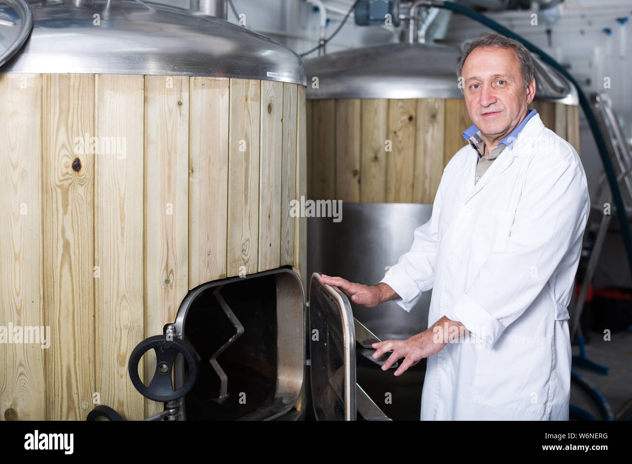 Brewer is standing near reservoir for beer on his workplace indoor ...
