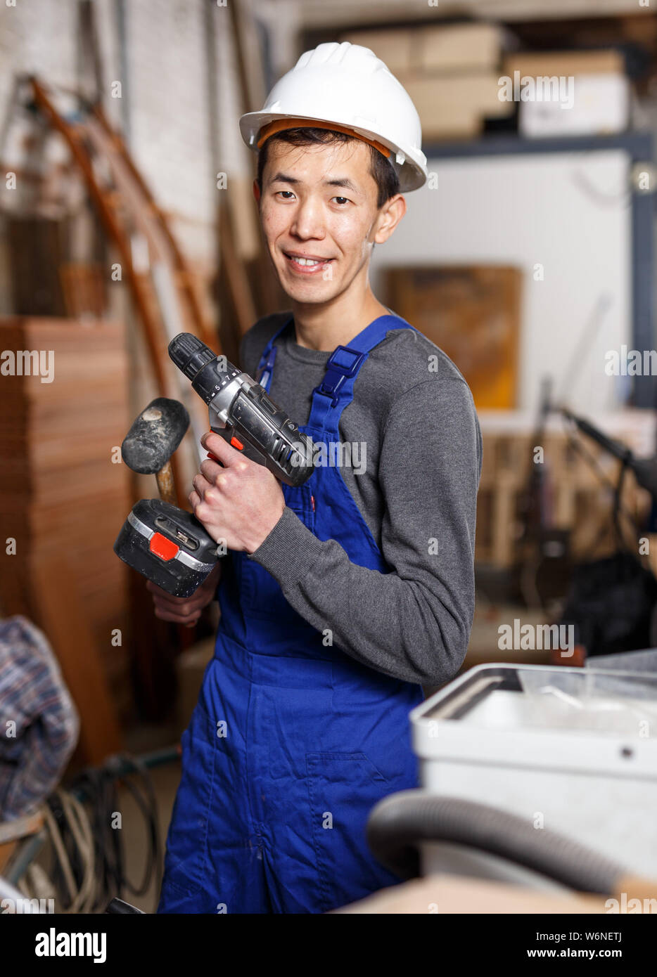 Asian worker in work wear holding power tools inside built cottage ...