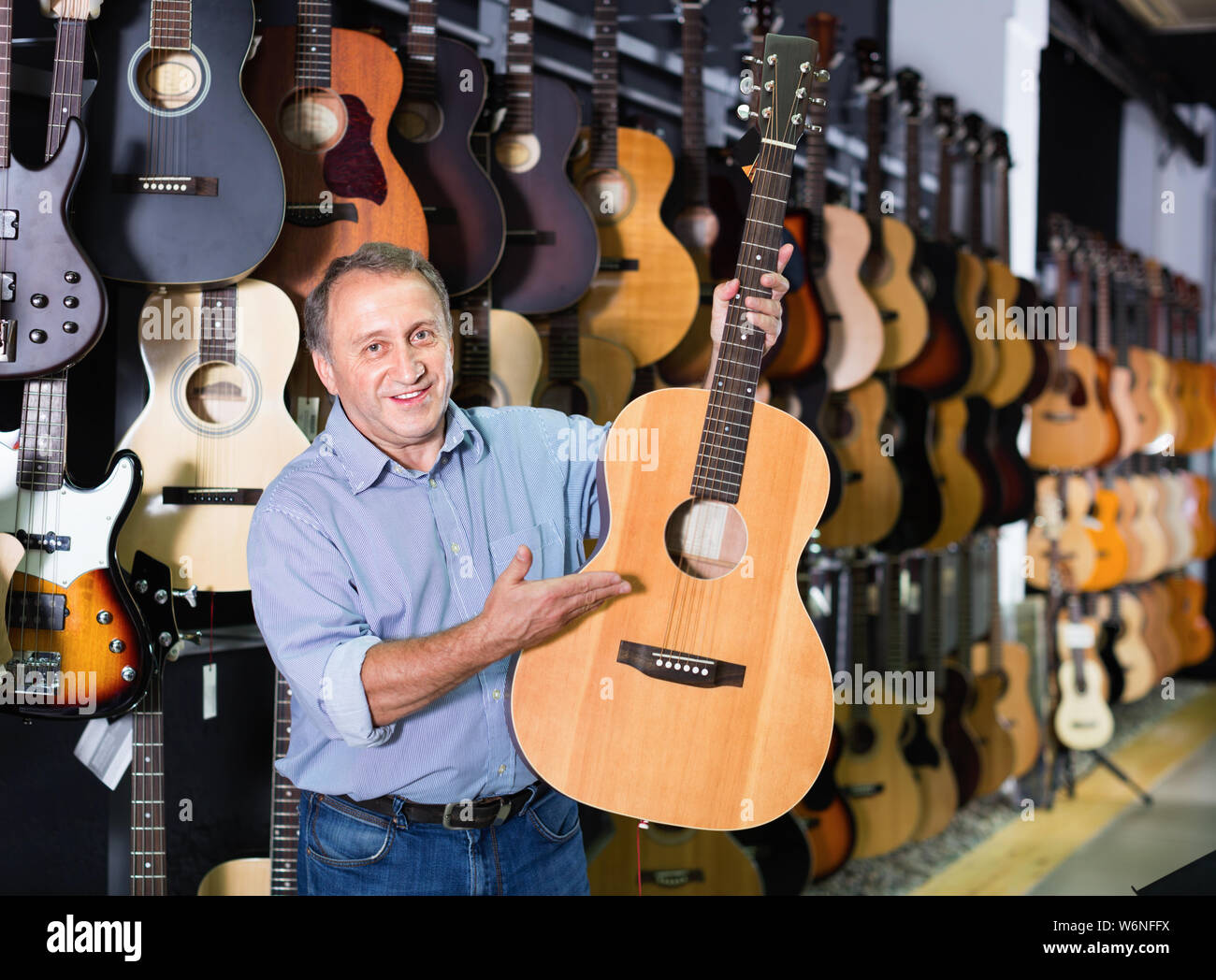 Adult cheerful positive smiling guitarist is standing with acoustic ...