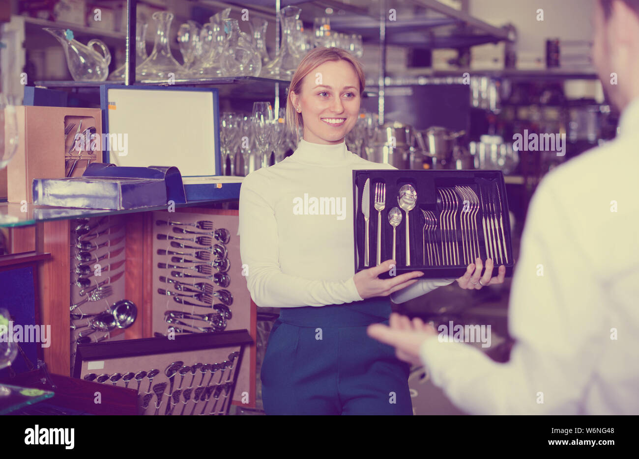 Happy cheerful female shopping assistant offering cutlery in dinnerware ...