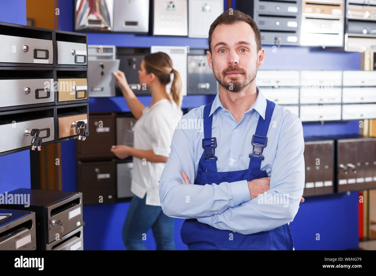 Confident salesman in blue overall standing in mailbox store Stock ...