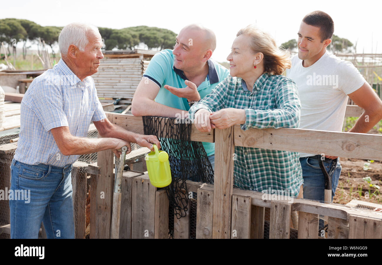 Family of four gardeners talking together near wooden fence in garden ...