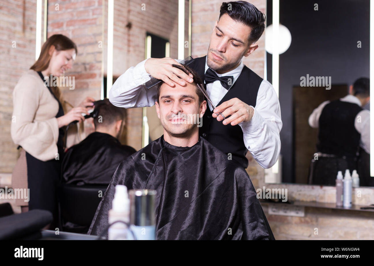 Skillful man barber making haircutting for male client in hair studio ...