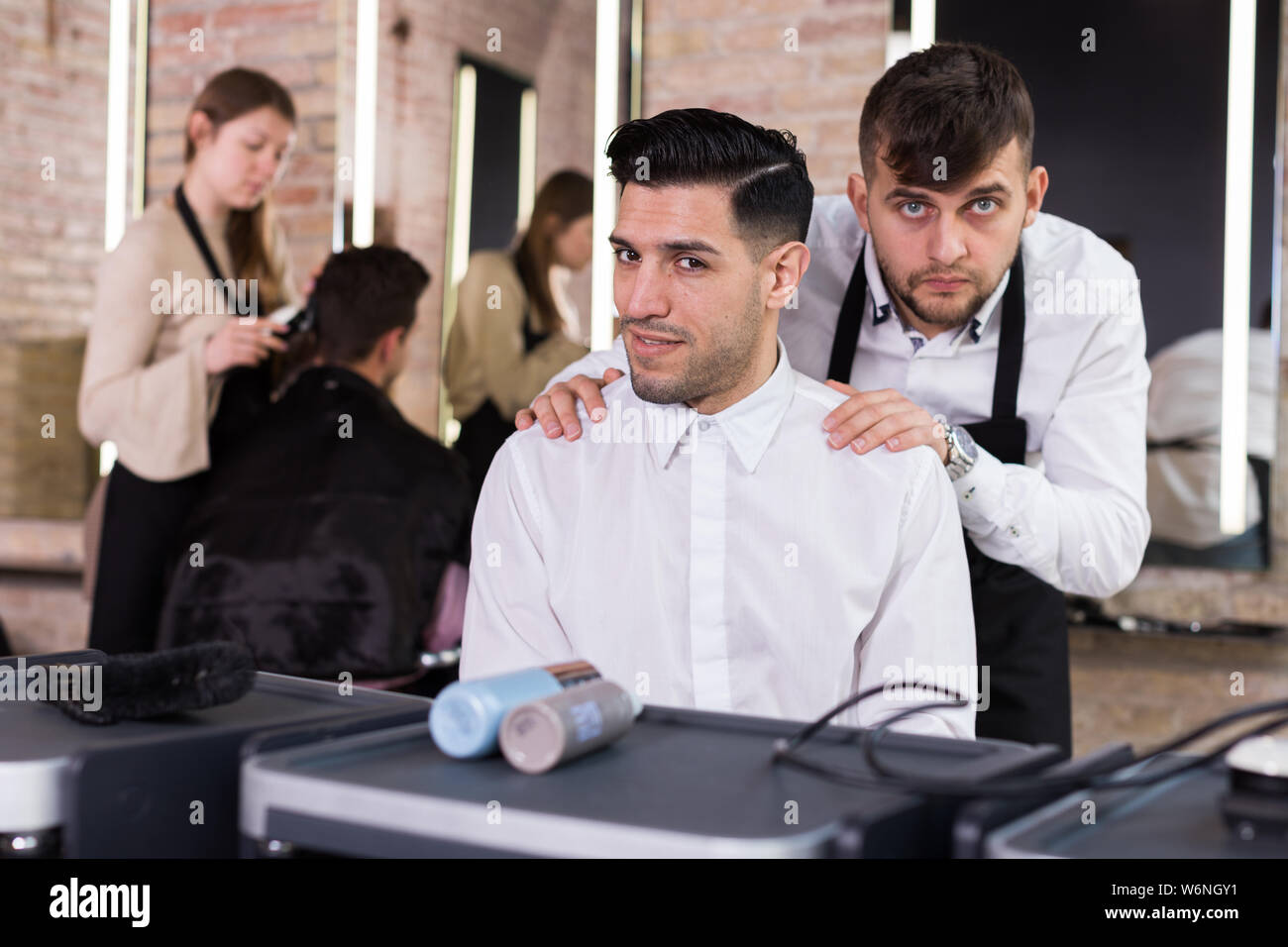 Skillful hairdresser finished haircut and showing result to pleased man ...