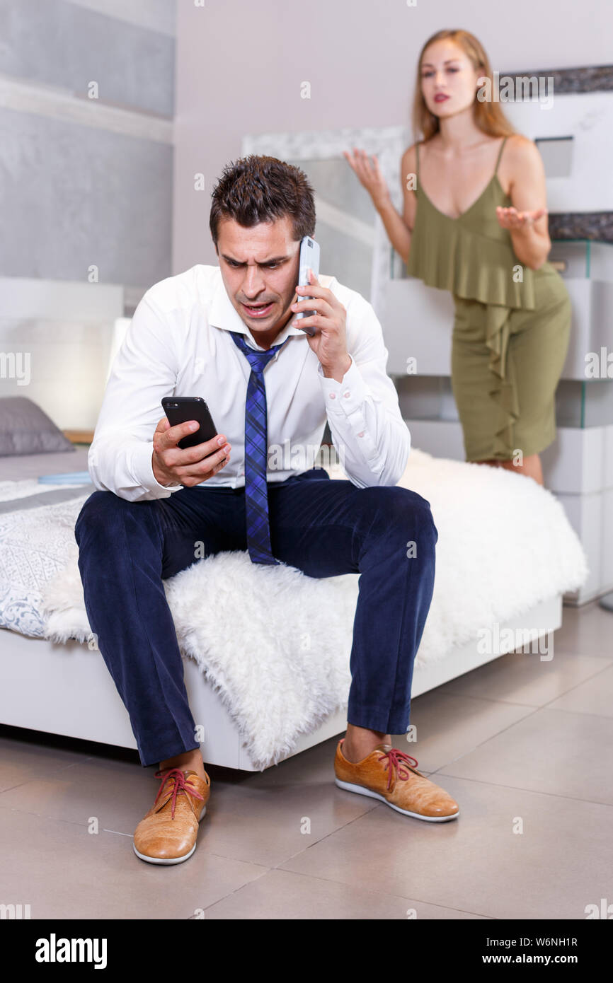 Furious man screaming on two mobile phones in bedroom on background ...