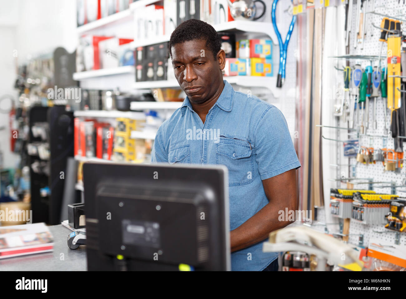 Confident African American salesman working on computer behind counter ...