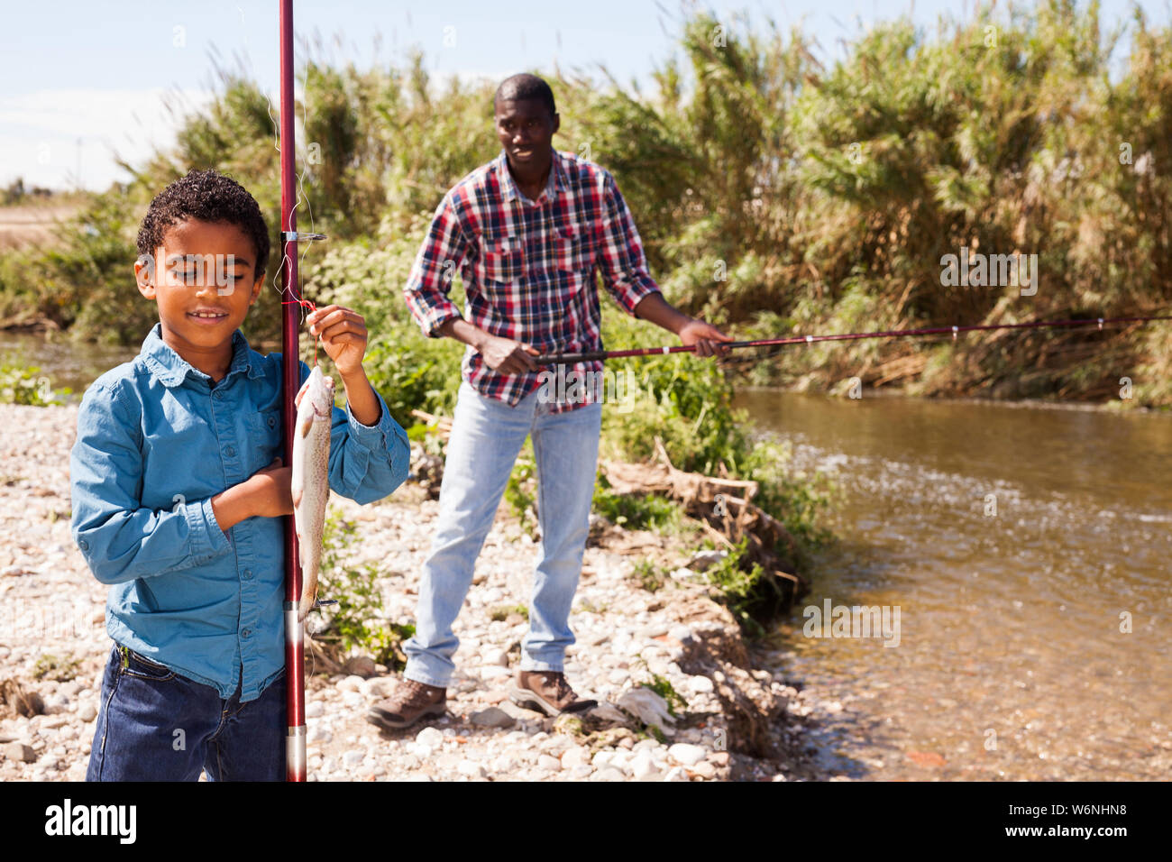 Portrait of afro fisherman and his little son holding fishing rod with ...