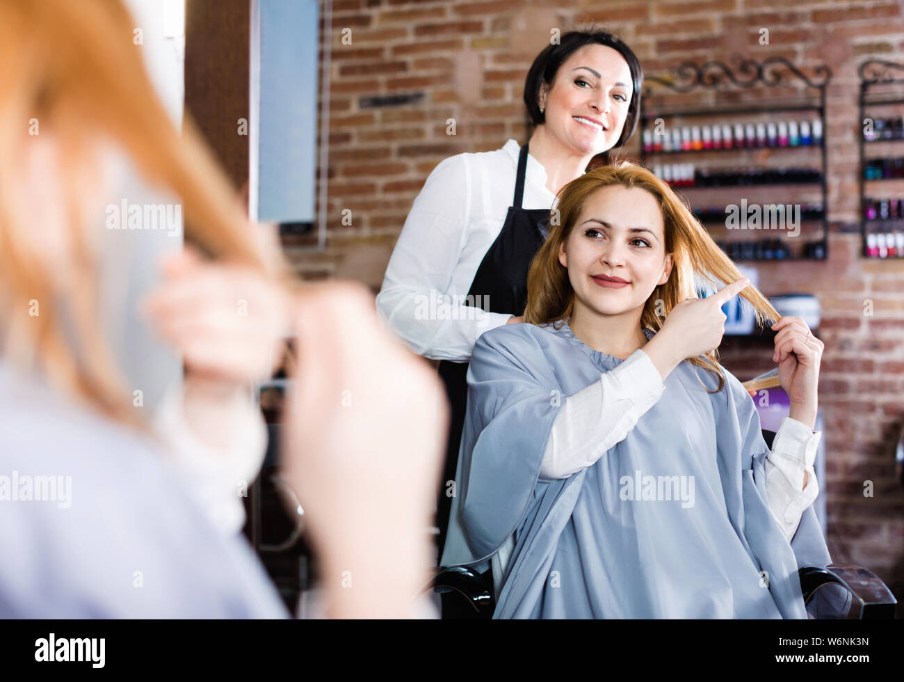 Young cheerful positive woman points to master in hairdress salon right ...