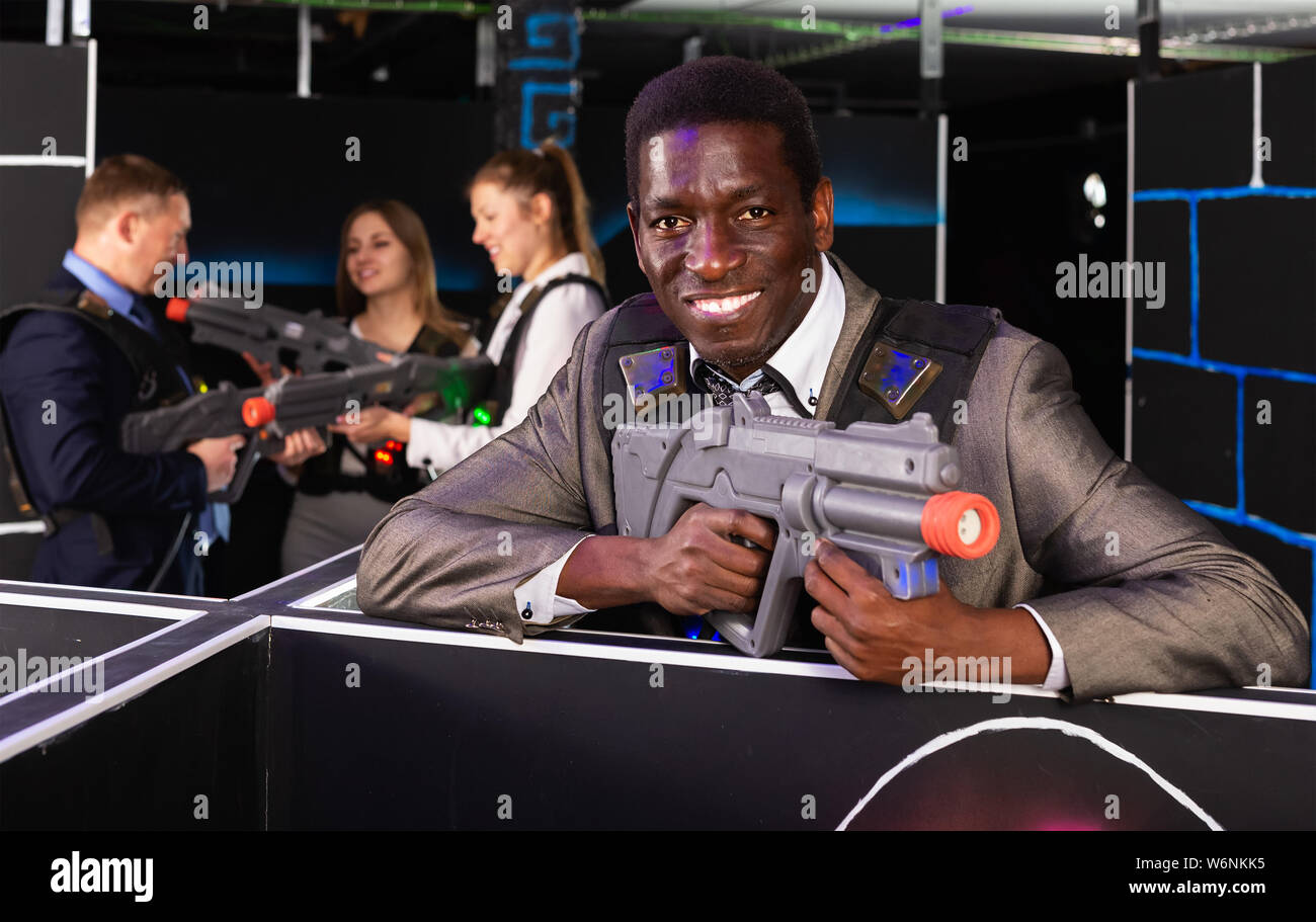 Portrait of Afro man playing laser tag with his co-workers on dark ...