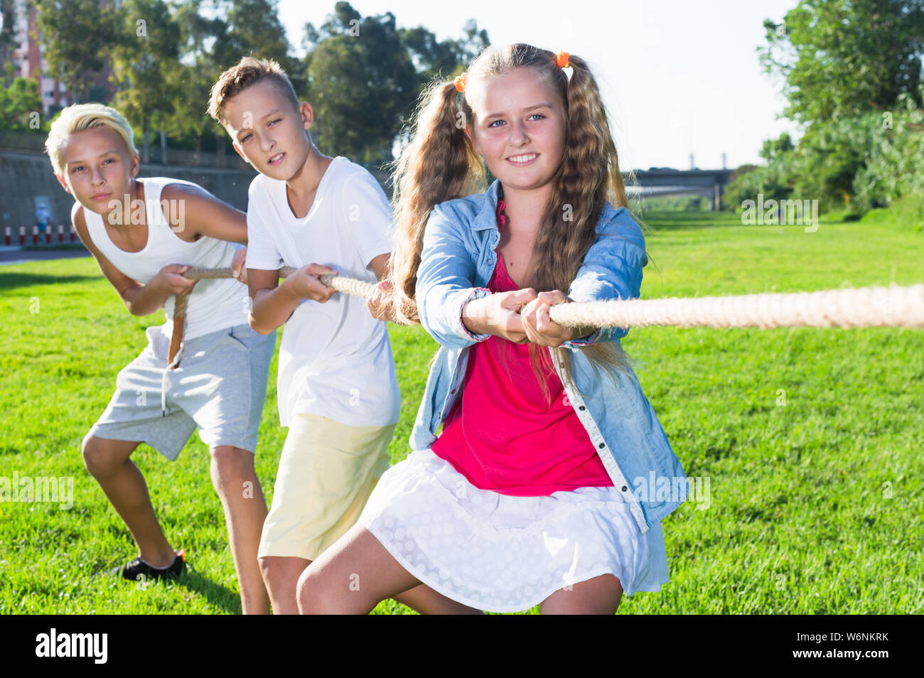 Group of laughing children having fun together outdoors pulling rope ...
