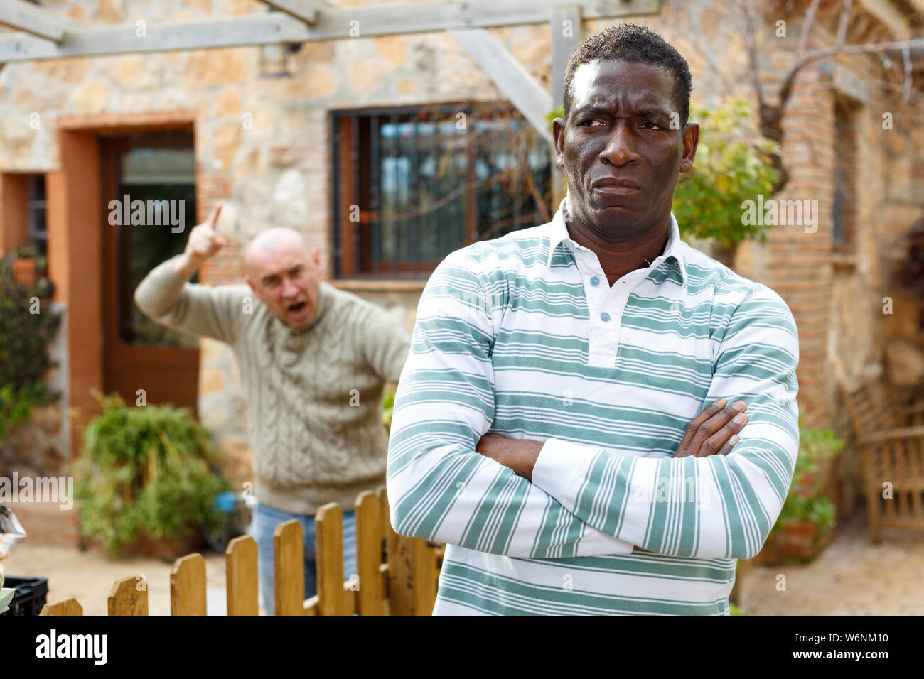 Disgruntled man ignoring his friend shouting in backyard of rural house ...