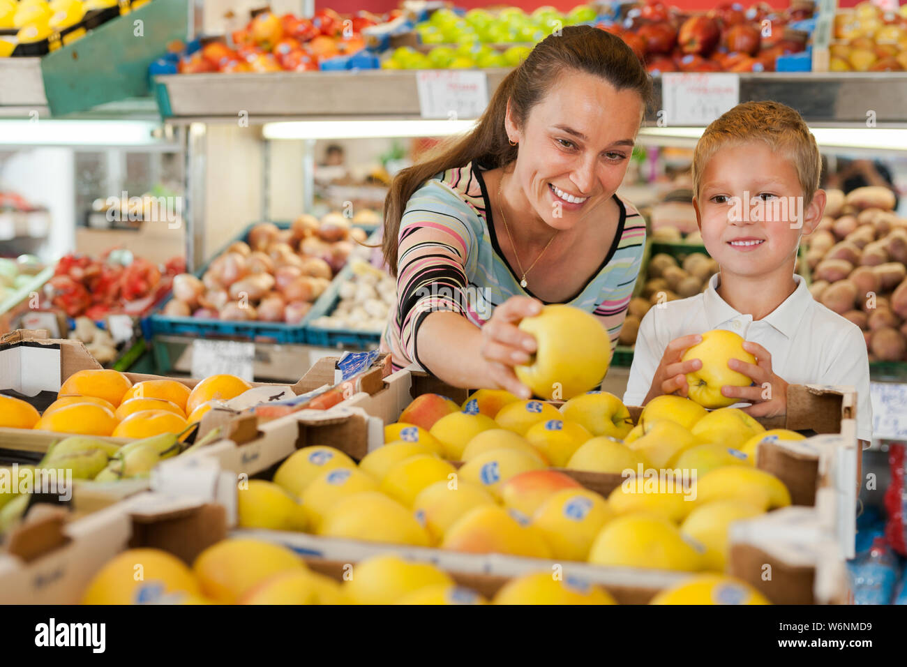 Portrait of little blonde boy and his happy mom buying pears and apples ...
