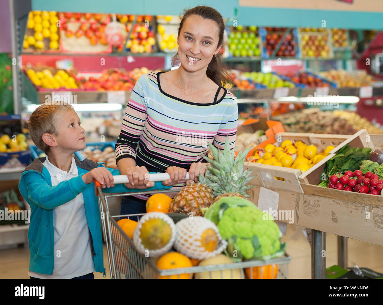 Cheerful mother with little boy buying fruits and vegetables at store ...