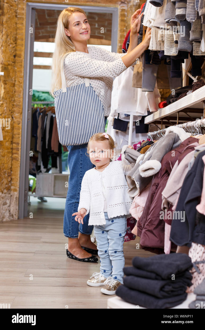 Cheerful young woman and her little daughter shopping in kids clothing ...