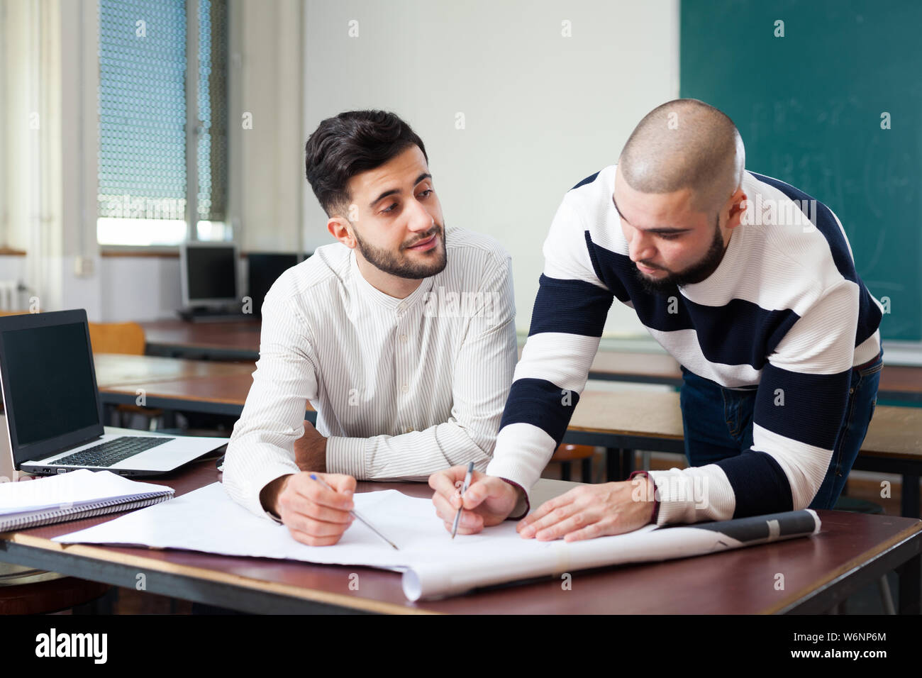 Portrait of two young guys working on their student project at desk in ...