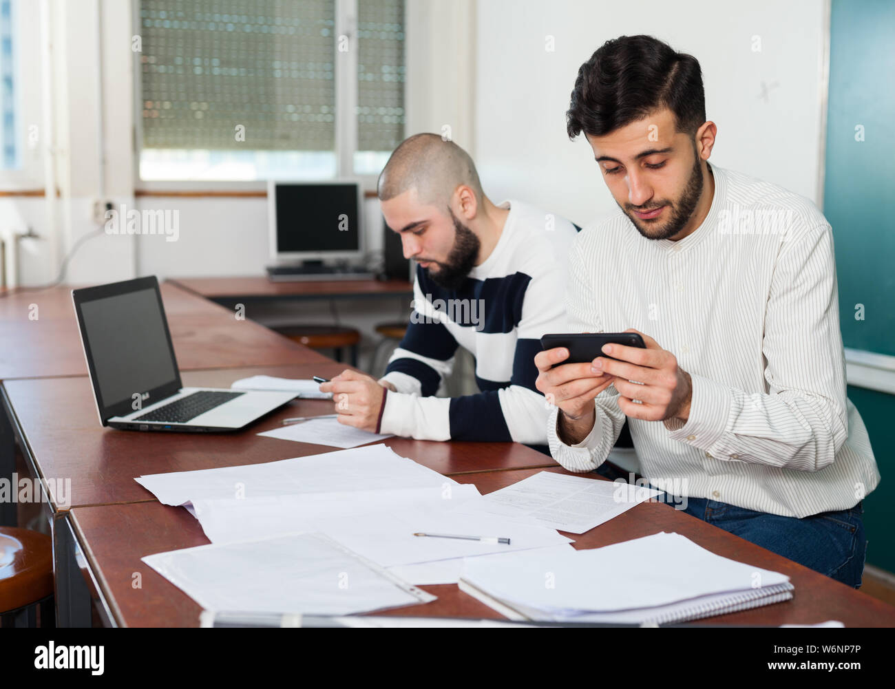Young student distracting from his studies and watching at smartphone ...