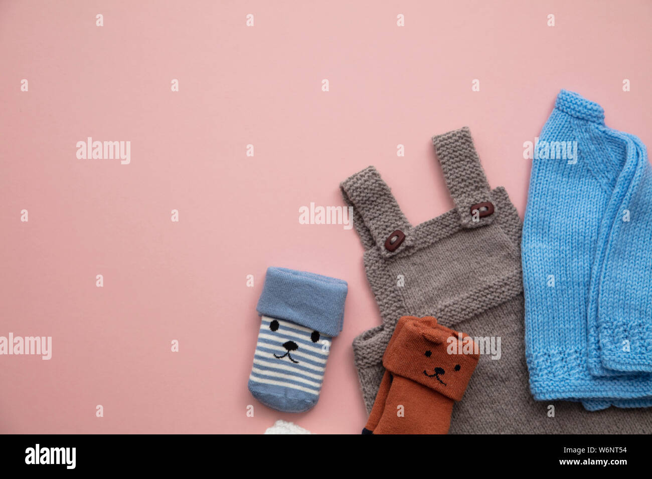 Cute handmade knitted baby clothes layout on a pastel pink background ...