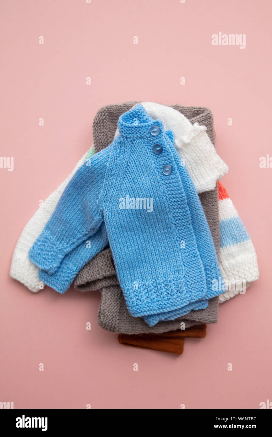 Cute handmade knitted baby clothes layout on a pastel pink background ...